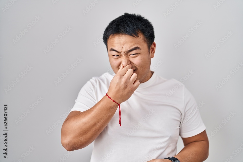 Young chinese man standing over white background smelling something ...