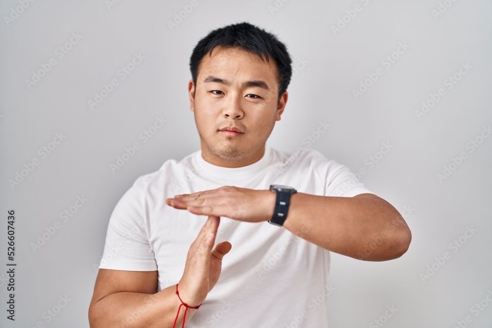 Young chinese man standing over white background doing time out gesture ...