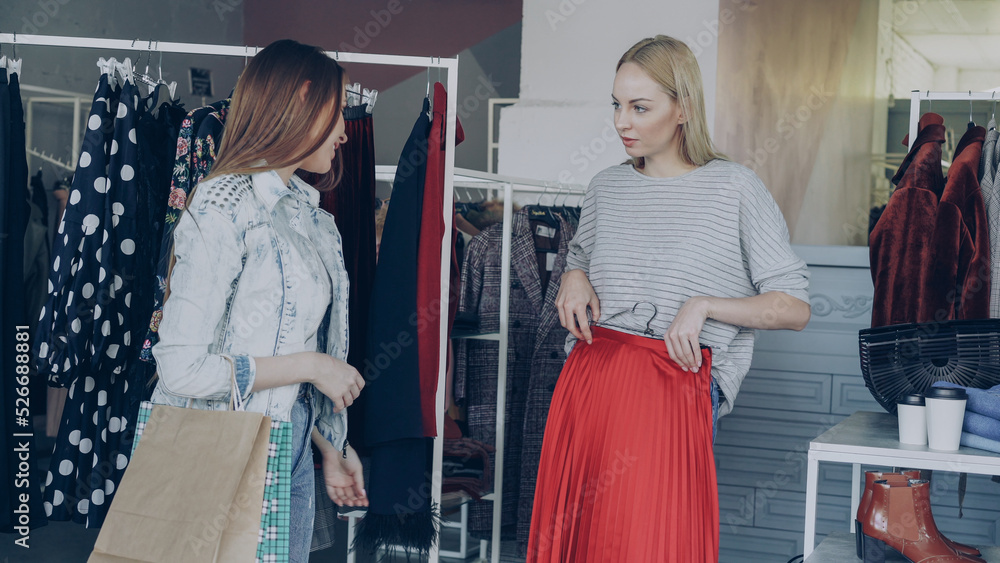 Girls are choosing clothes together while standing near rails in ...