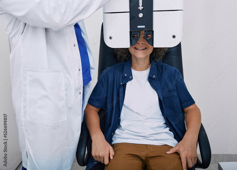 Teenager boy has eye test in ophthalmological clinic using phoropter ...