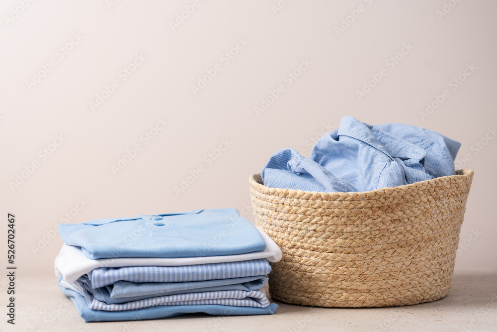 Stack of shirts and wicker basket with clothes on beige background ...