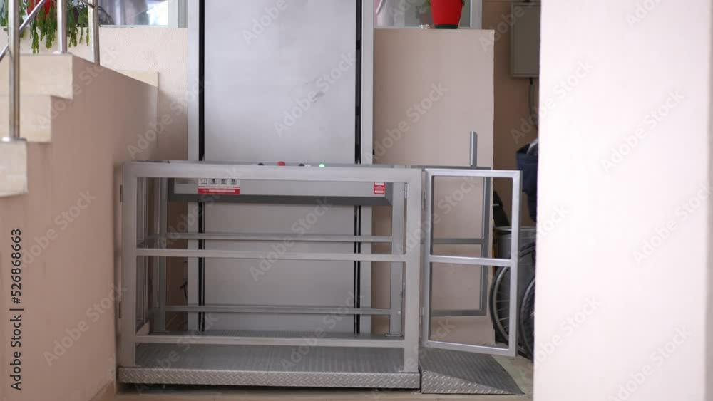 Wide shot man riding wheelchair leaving lift platform entering building ...