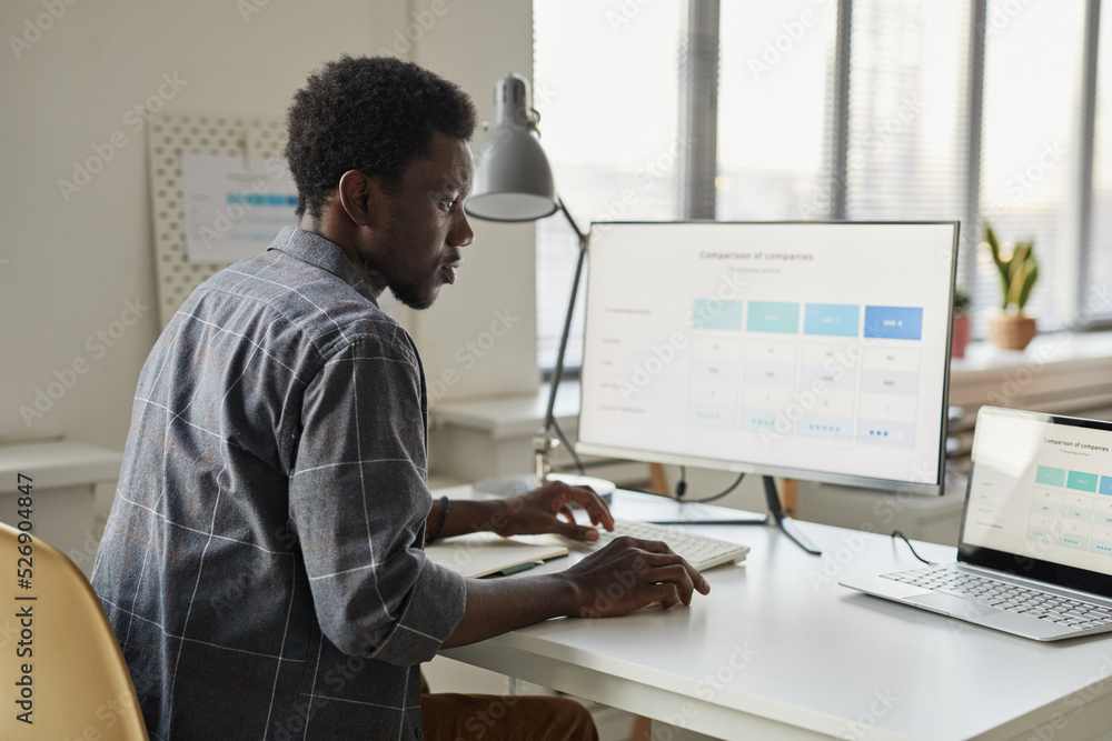 Minimal side view at young black man using computer at workplace in ...