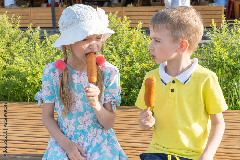 Hungry children eating street food sitting on a park bench. A boy and a ...