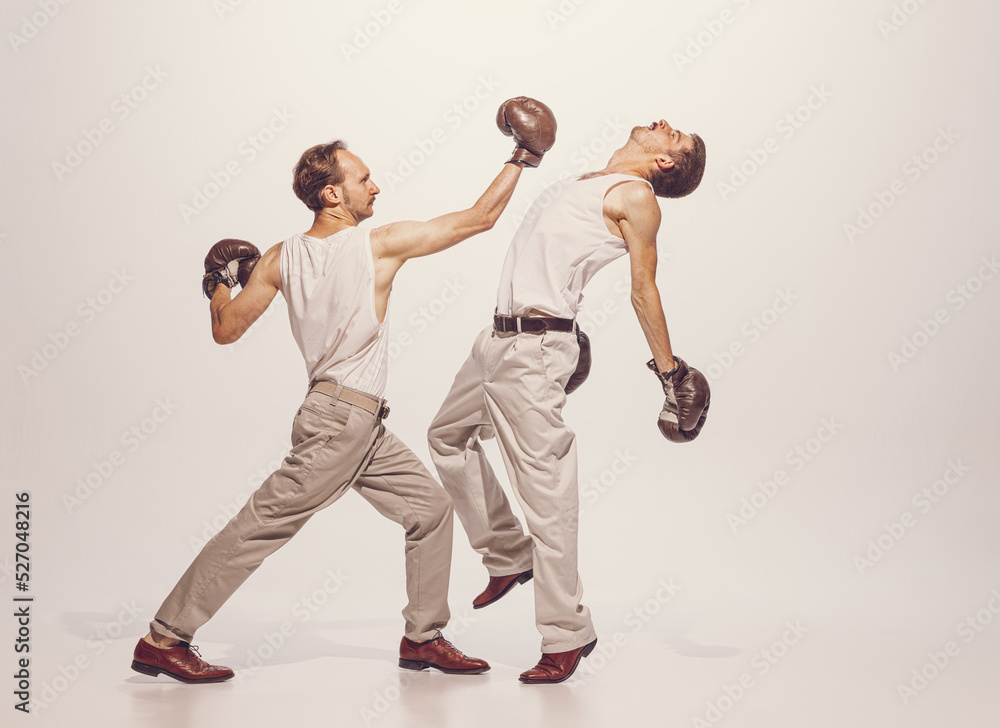 Portrait of two men playing, boxing in gloves isolated over grey studio ...