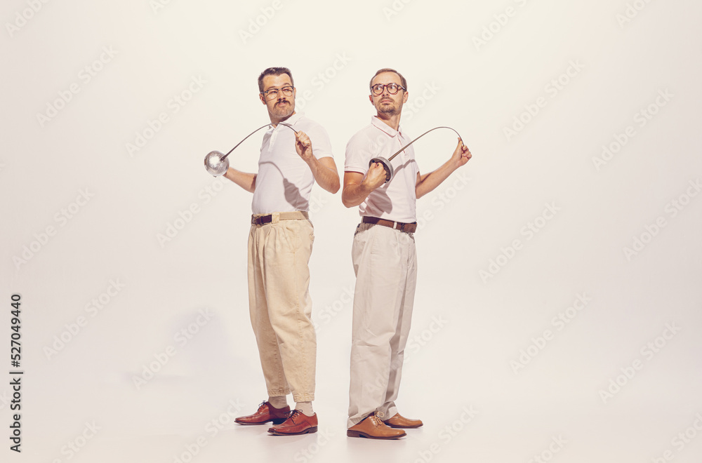 Portrait of two men in a suit posing with swords isolated over grey ...