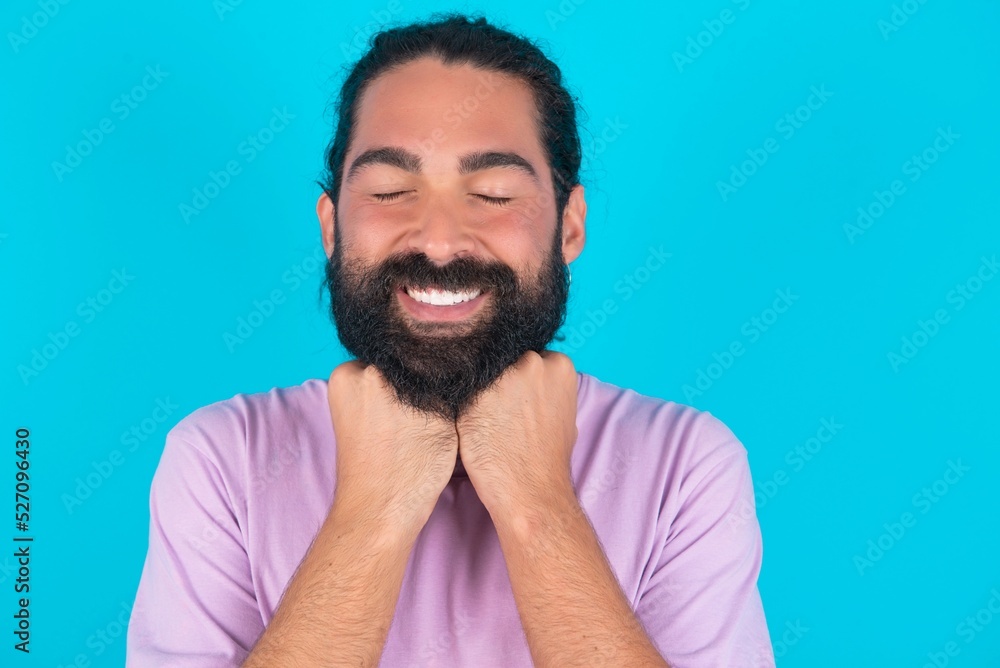 Cheerful young bearded man wearing violet T-shirt over blue studio ...