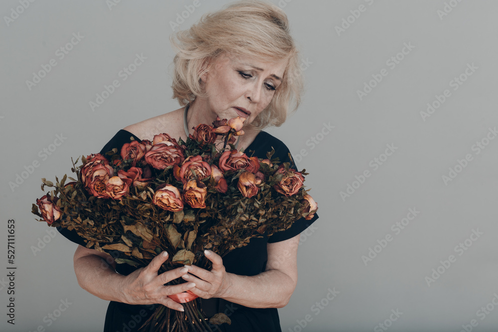 Sad elderly senior woman in white shirt holds withered one dry old dead ...