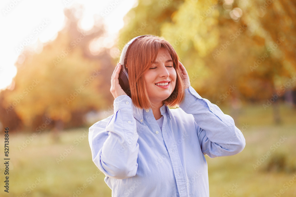 Young smiling woman listening music with headphones at sunset ...