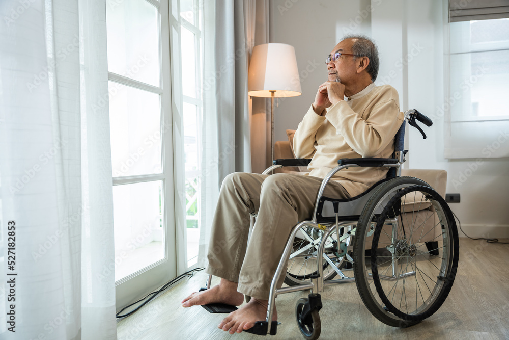 Asian senior man disabled sitting alone in wheelchair looking through window at hospital, lonely ...