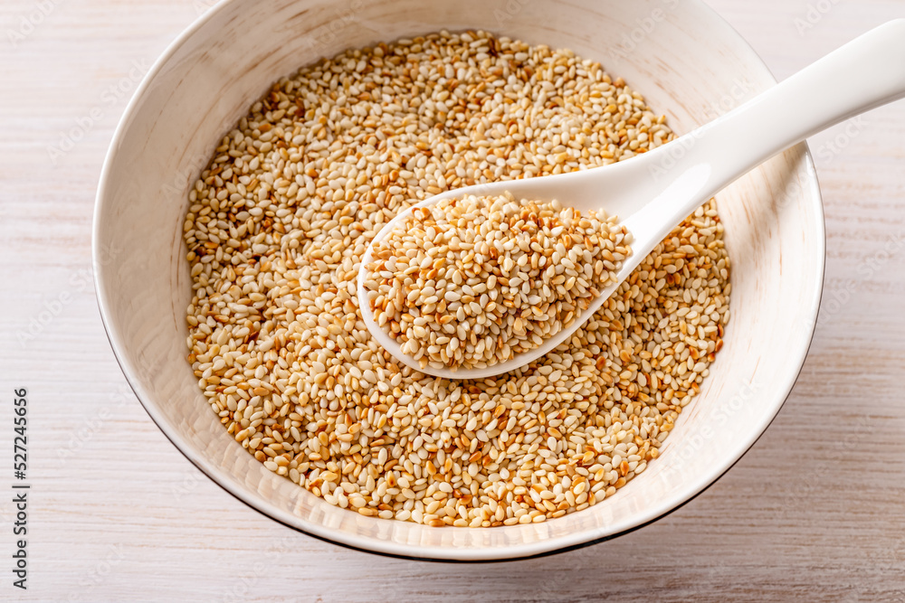 Toasted sesame seeds and white spoon in a porcelain bowl. Roasted ...