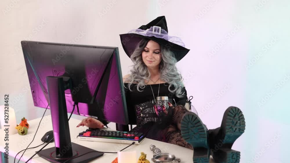 Beautiful witch sits at the computer with cozy Halloween decorations ...