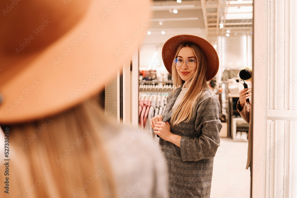 A smiling young shopaholic woman tries on clothes in a shopping mall ...