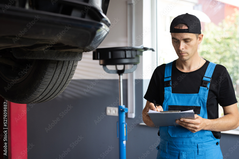 Mechanic inspects the car undercarriage way and makes a note on his ...