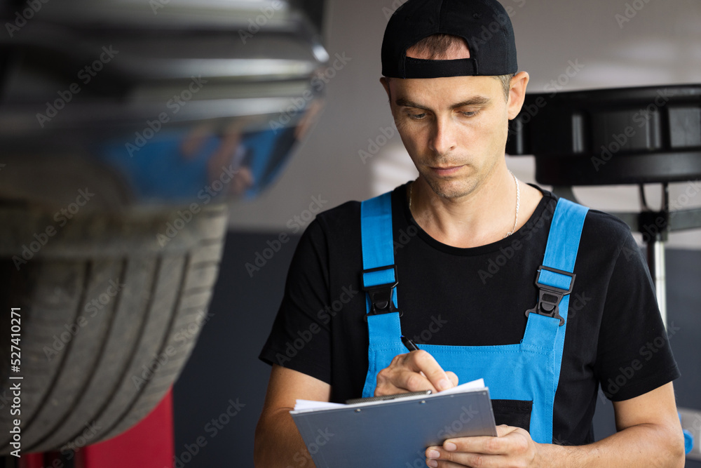 Mechanic inspects the car undercarriage way and makes a note on his ...