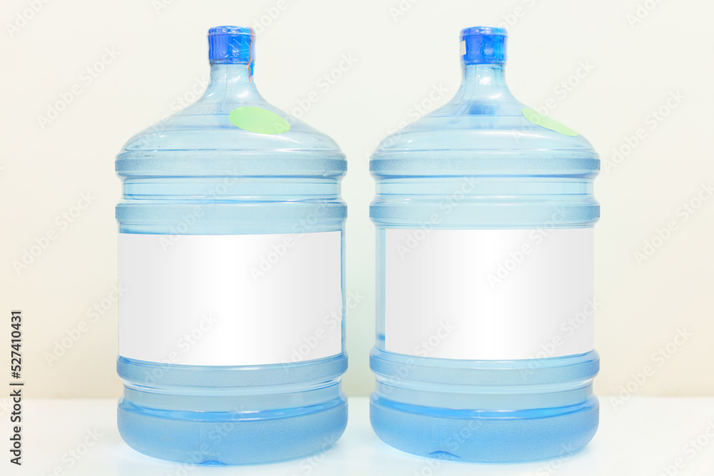 Two plastic gallon water bottle containers with white labels stand on a ...