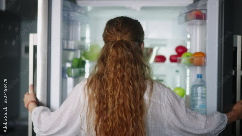 Young woman taking vegetables from fridge and has fun singing and ...