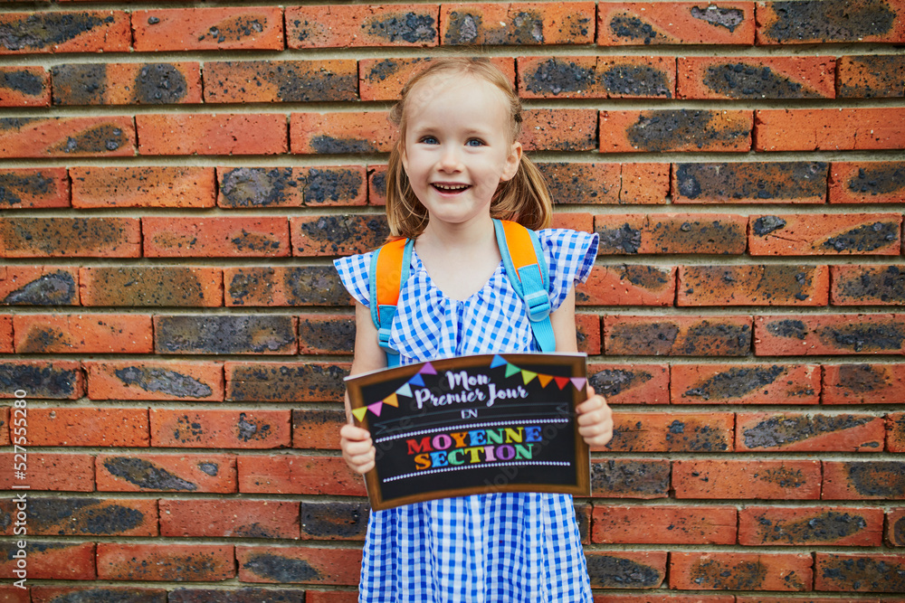 Cheerful 4 years old girl holding a poster with text "My first day in ...
