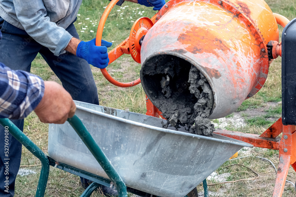 A worker pours cement mortar, concrete, from a concrete mixer into a ...