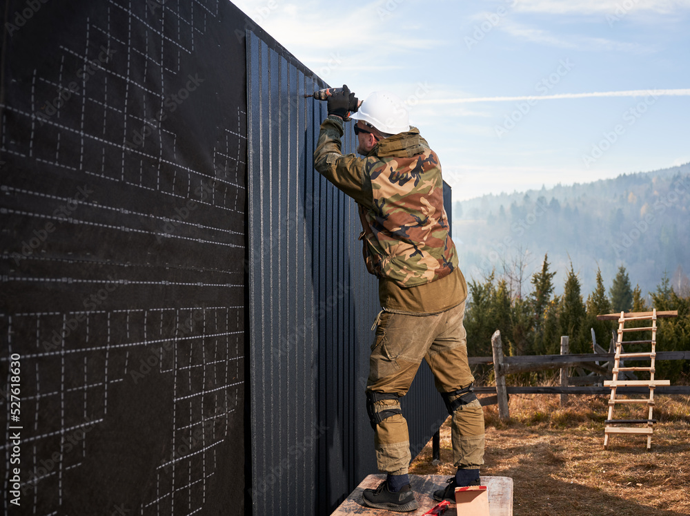 Male builder installing black corrugated iron sheet used as facade of ...