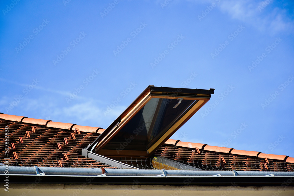 top hung roof window closeup view on sloped clay tile house roof. blue ...