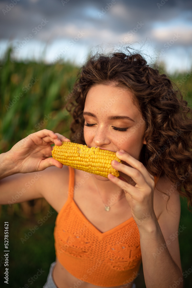 Girl with corn in a cornfield. The girl eats corn on the background of ...
