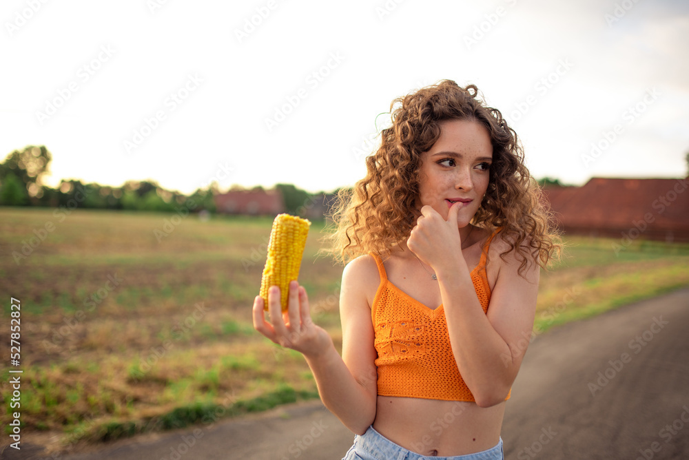 Girl with corn in a cornfield. The girl eats corn on the background of ...