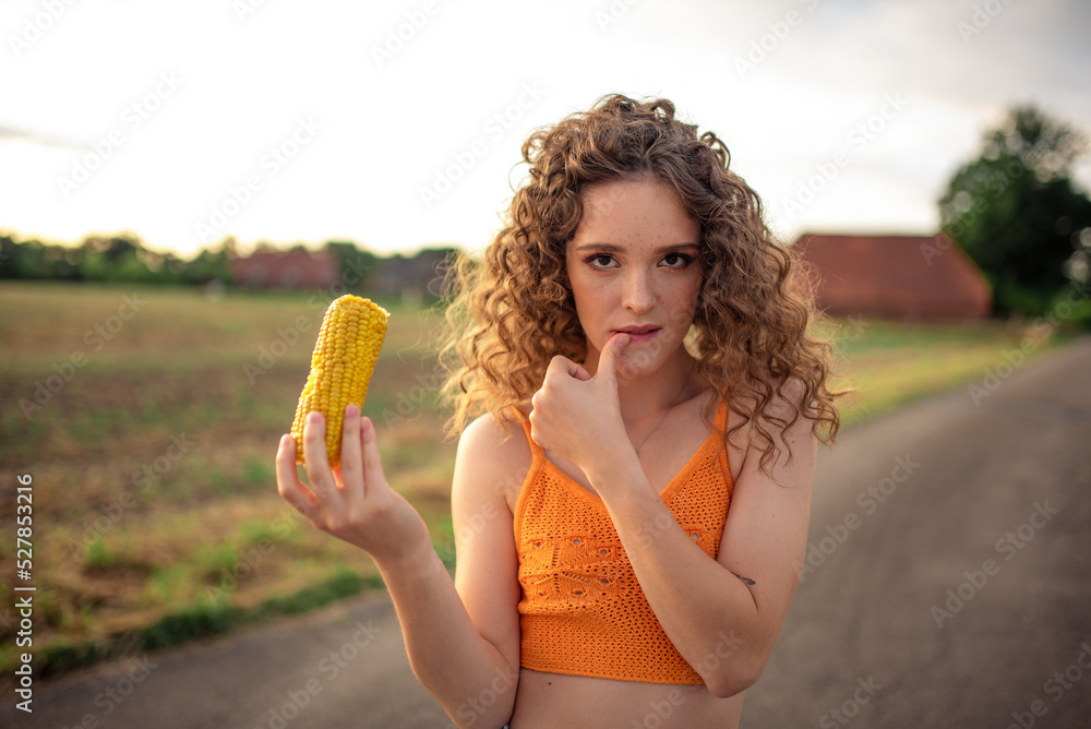 Girl with corn in a cornfield. The girl eats corn on the background of ...