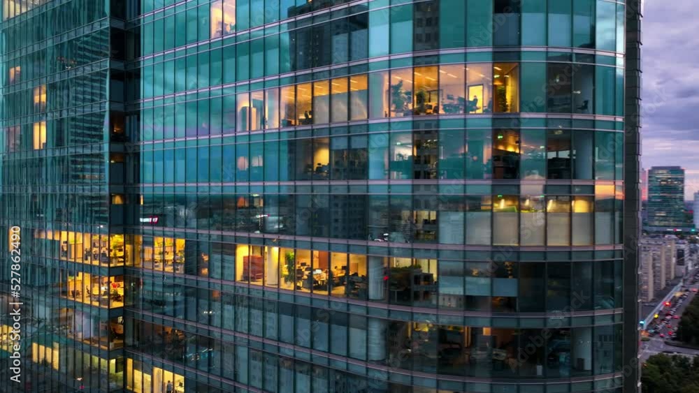 flying around a modern glass skyscraper at night with illuminated ...
