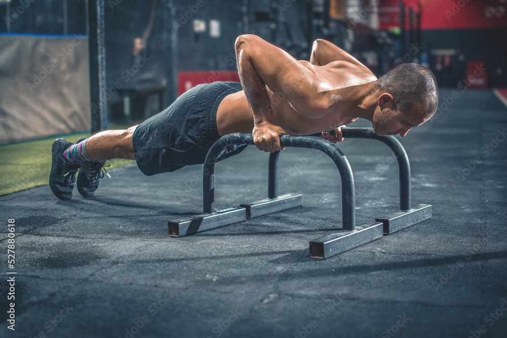 Fit and muscular man doing horizontal push-ups with parallel bars in ...