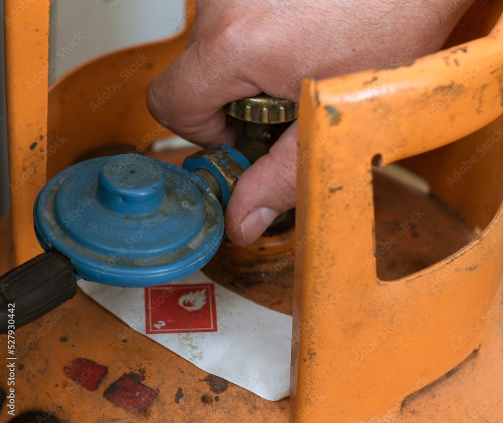 Man's hand operating valve orange LPG cooking gas cylinder. The picture ...