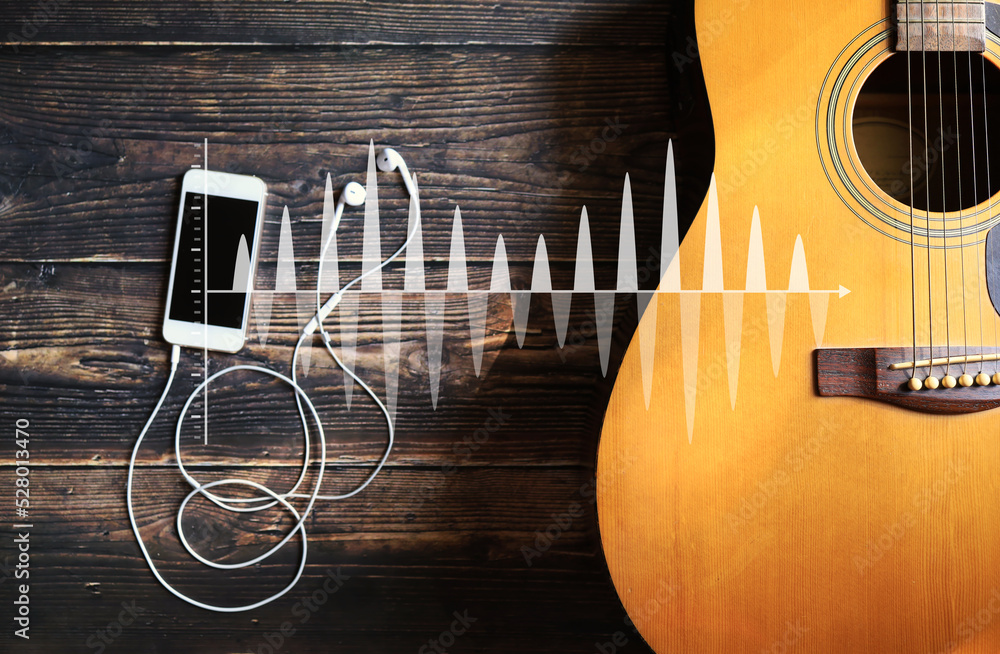 Acoustic guitar on the wooden background and the white ear phone smart ...