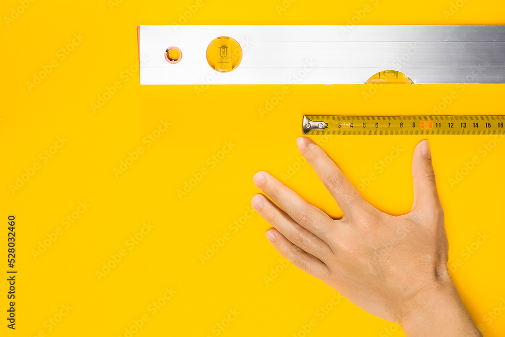 Hand, measure tape and aluminium spirit level tool on yellow background ...