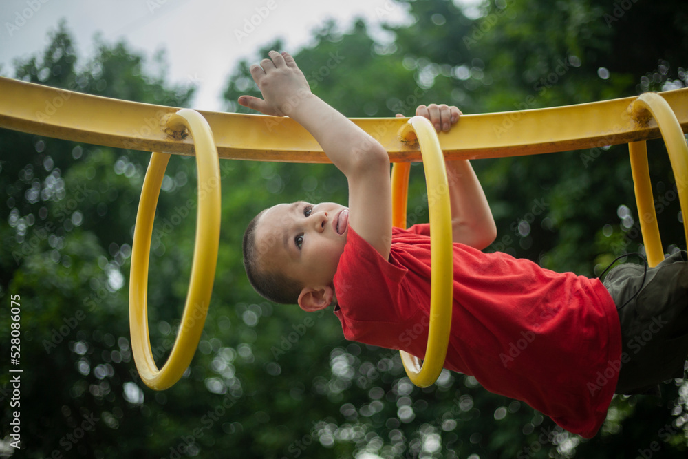 Boy on playground climbs through rings. Child plays at height. Sports ...
