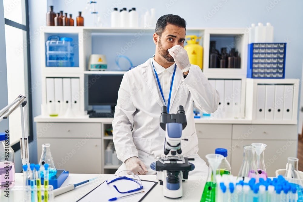 Young hispanic man with beard working at scientist laboratory smelling ...