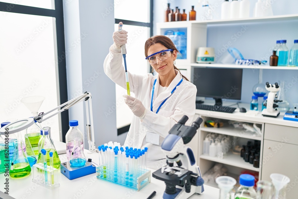 Young hispanic woman wearing scientist uniform using pipette at ...
