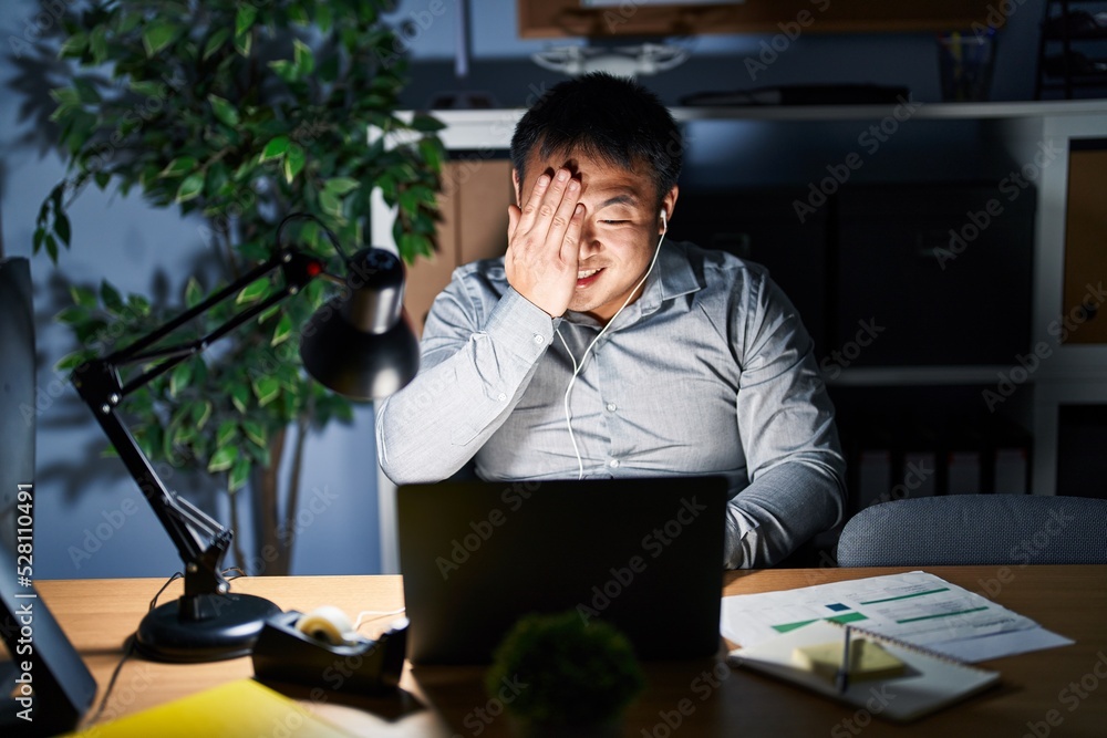 Young chinese man working using computer laptop at night covering one ...