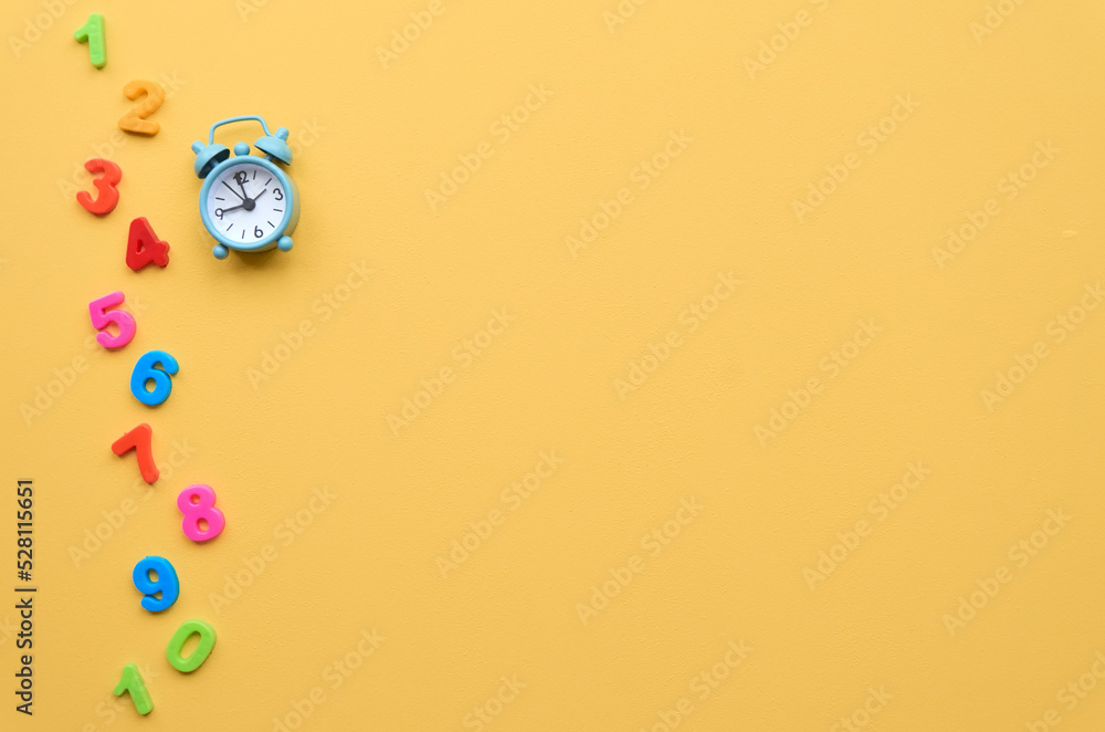 Small alarm clock, numbers on yellow background, flat lay top view ...