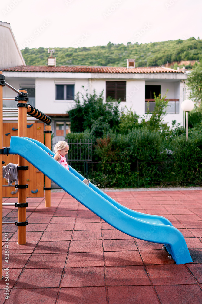 Little girl slides down a slide on a playground. Side view. High ...