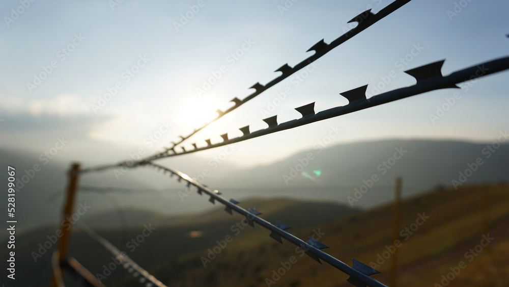 Sharp barbed wire on the fence with a blurred background of mountains ...