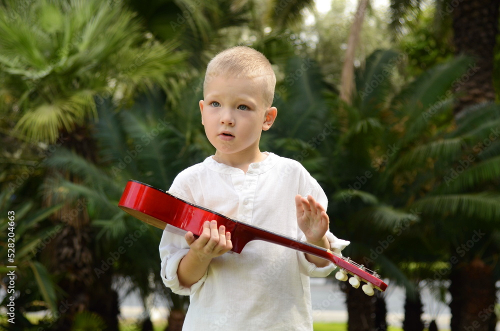 Little boy plays the acoustic guitar in the park. The child learns to ...