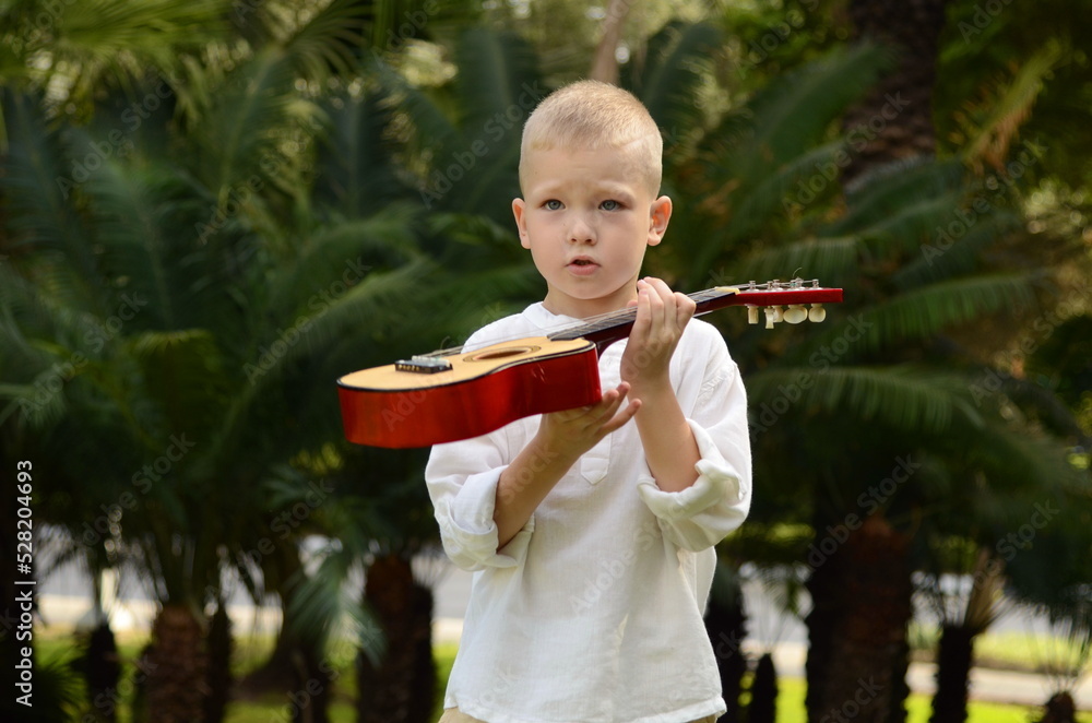 Little boy plays the acoustic guitar in the park. The child learns to ...