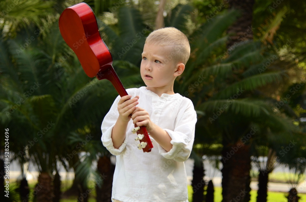 Little boy plays the acoustic guitar in the park. The child learns to ...