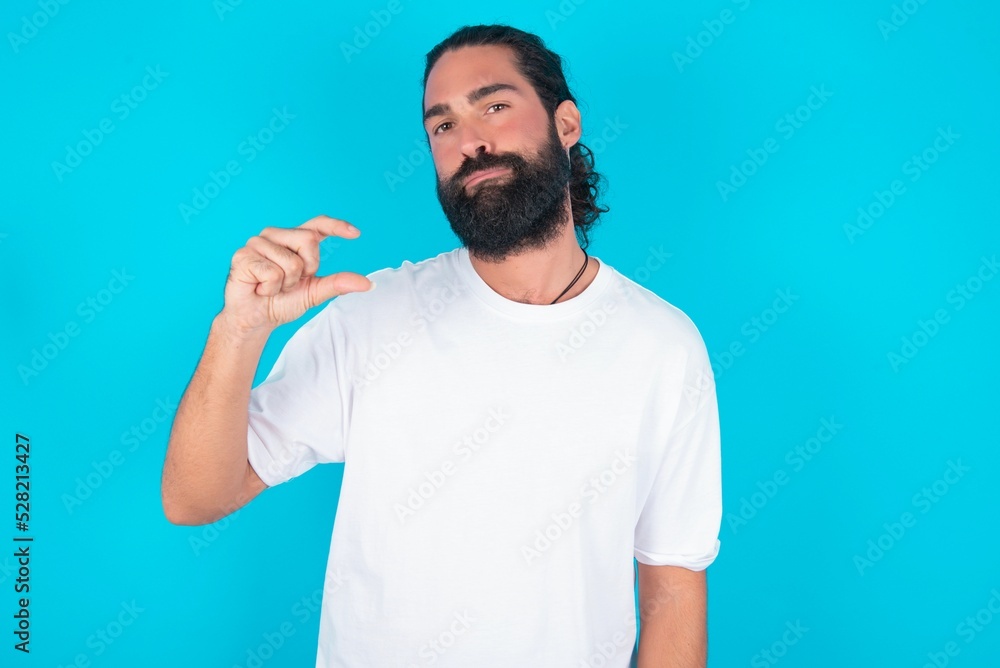 Displeased young bearded man wearing white T-shirt over blue studio ...