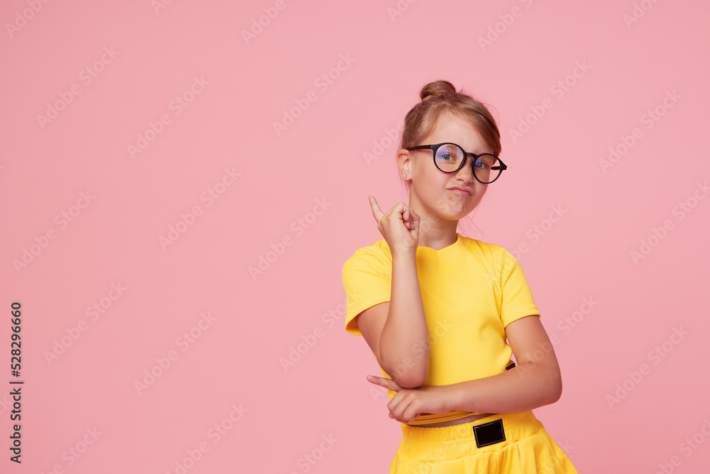 Smart child girl in yellow clothes with eyeglasses on a pink background ...