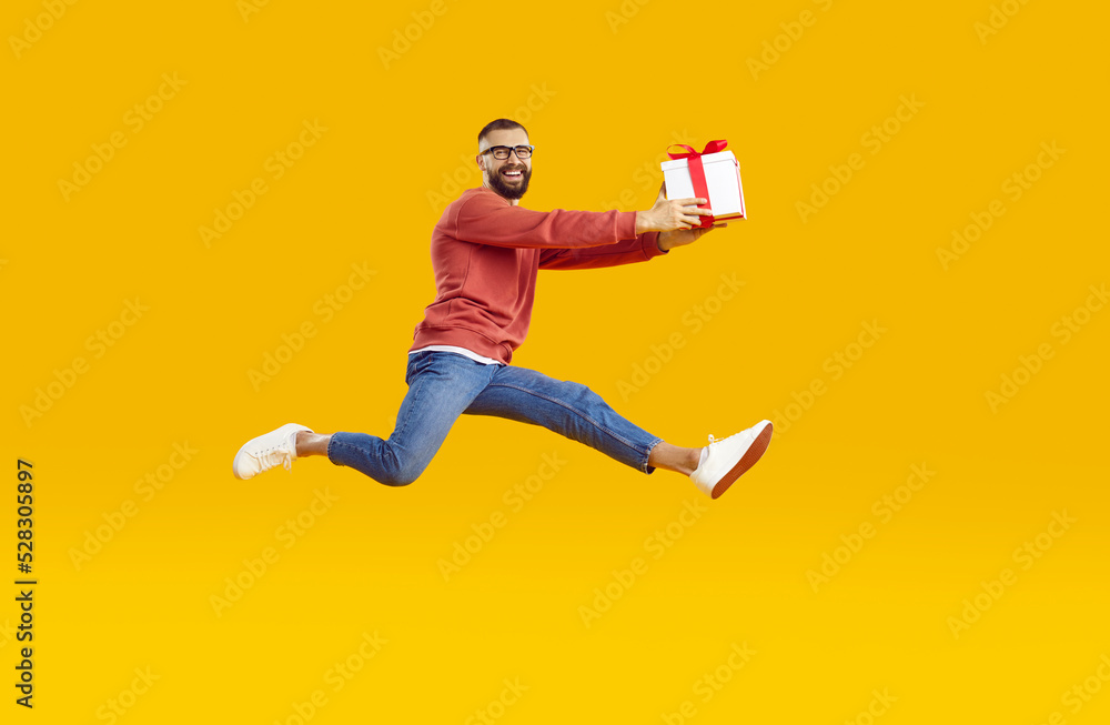 Handsome man in casual clothes and glasses holding gift box and jumping ...