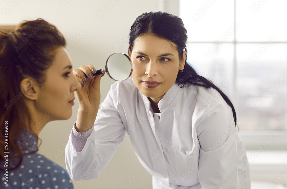 Female doctor looking at patient's skin through magnifying glass ...