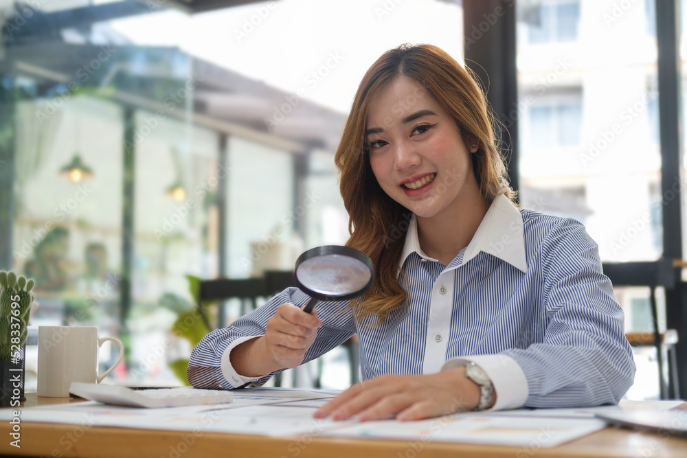 Businesswoman examining documents with a magnifying glass at her office ...