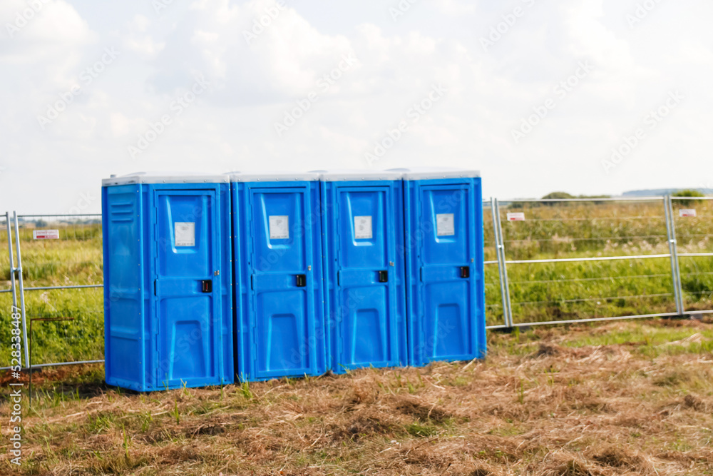 Defocus four blue of portable bio toilet cabins in field. Line of ...