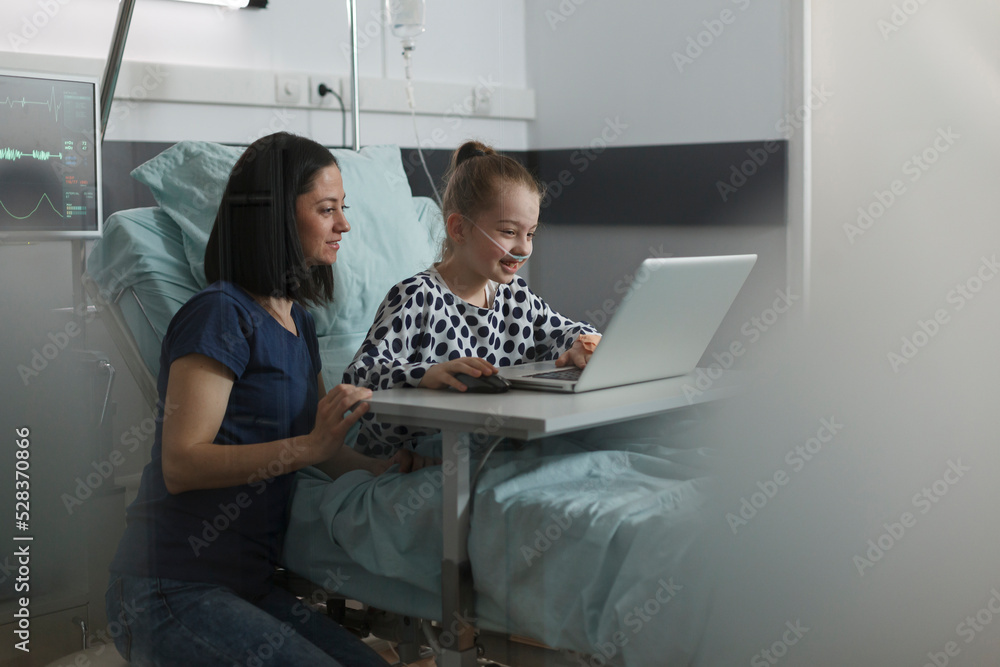 Joyful child under treatment gaming on patient bed while parent takes ...